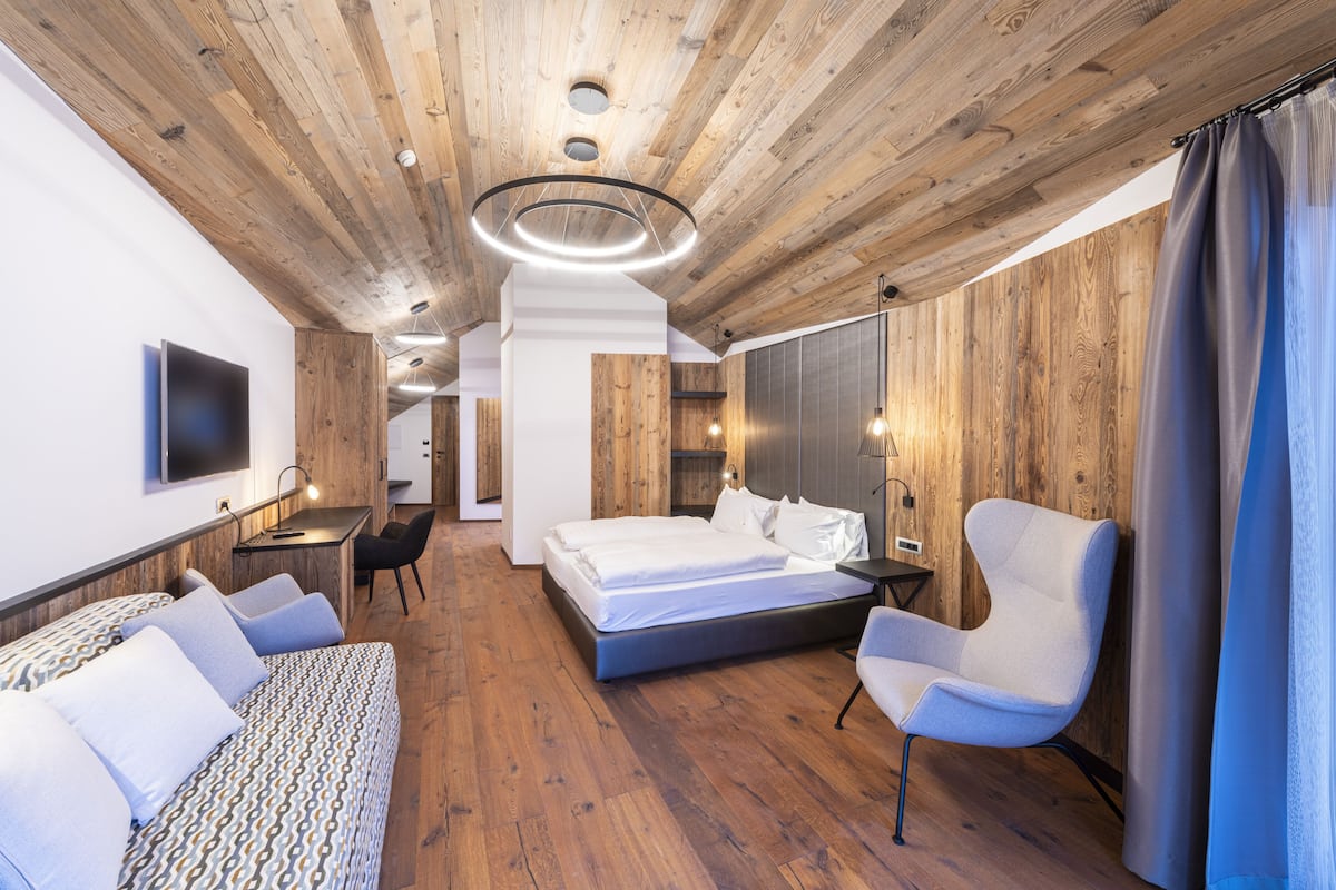Quarto de hotel moderno com teto de madeira, uma cama grande, escrivaninha e uma cadeira.