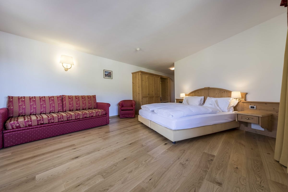 Um quarto com uma cama, um sofá vermelho, um guarda-roupa de madeira e uma mesa de cabeceira.