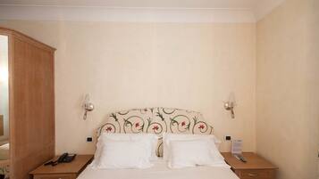 Quarto de hotel com uma cama, duas mesas de cabeceira, um criado-mudo, um espelho e um guarda-roupa de madeira.