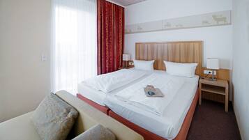 Quarto de hotel com uma cama grande, cabeceira de madeira, duas mesas de cabeceira com luminárias, cortina vermelha e parede com silhuetas de animais.