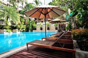 Uma área à beira da piscina com espreguiçadeiras e guarda-sóis, rodeada por vegetação exuberante e uma piscina azul cristalina.