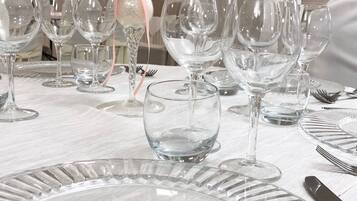Mesa posta com copos e pratos de vidro transparente, um vaso com flores brancas e uma fita cor-de-rosa.