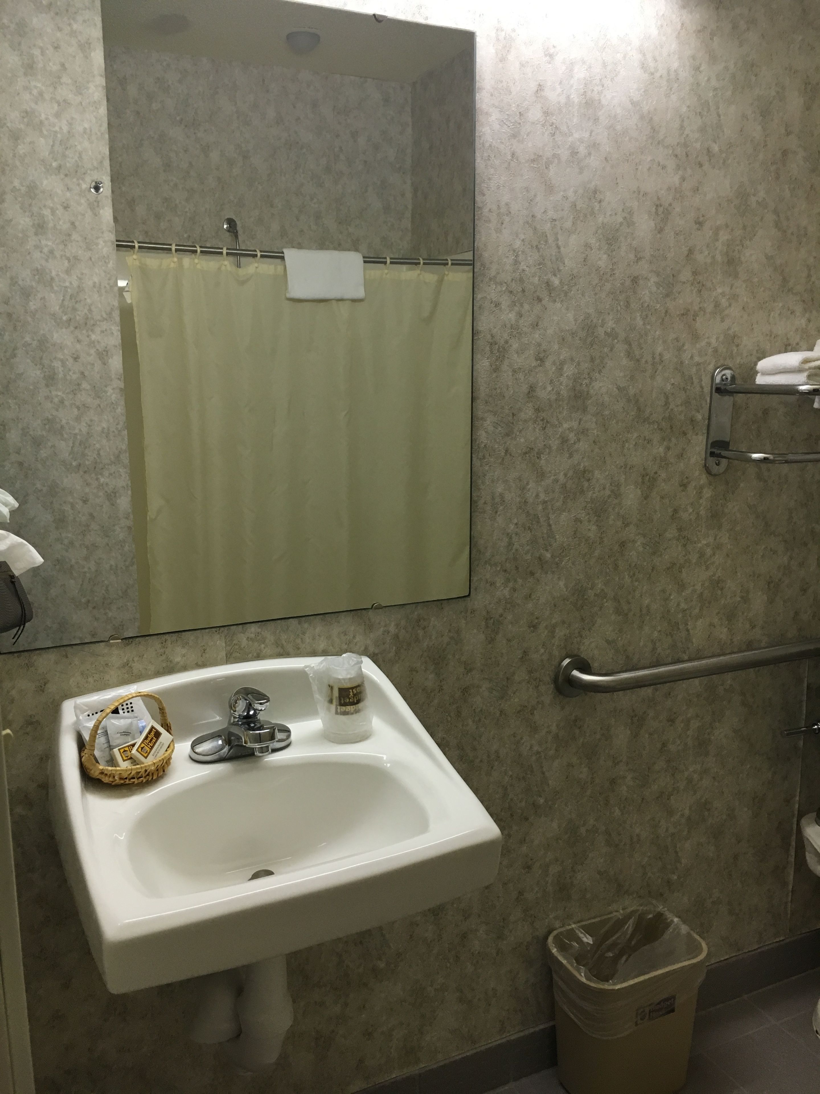 Casa de banho com lavatório branco, espelho, porta-toalhas e um cesto de lixo.