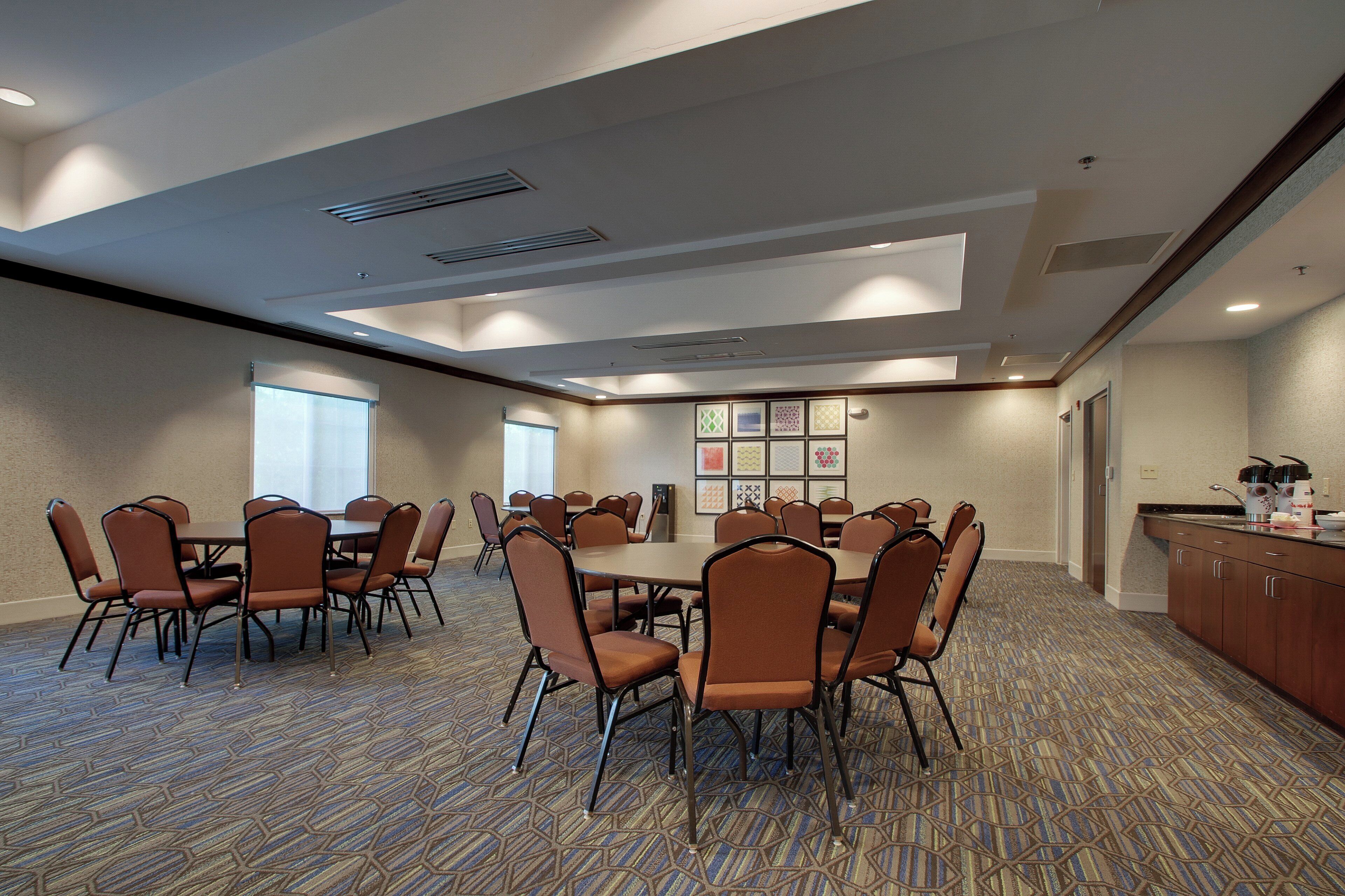 Sala de conferência com uma mesa grande e várias cadeiras, piso coberto de carpete e dutos de ventilação no teto.