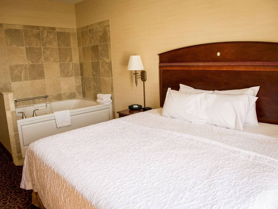 Quarto de hotel com uma cama grande, uma banheira e uma mesa de cabeceira com abajur.