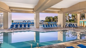 Área da piscina com cadeiras de descanso azuis e vista para o mar.