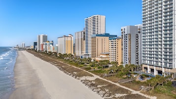 Um hotel costeiro com vários edifícios altos, uma praia de areia e um céu azul límpido.