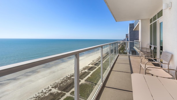Uma varanda com vista para a praia e o oceano, uma mesa e cadeiras.
