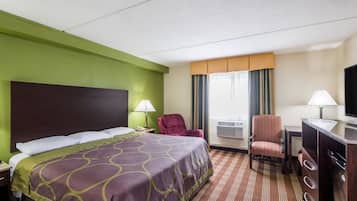 Quarto de hotel com cama, duas cadeiras, escrivaninha, televisão e ar condicionado.