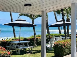 Uma área externa com mesas, cadeiras, guarda-sóis e vista para o mar.