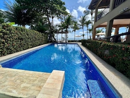 Piscina com borda azulejada, rodeada por vegetação exuberante e palmeiras.