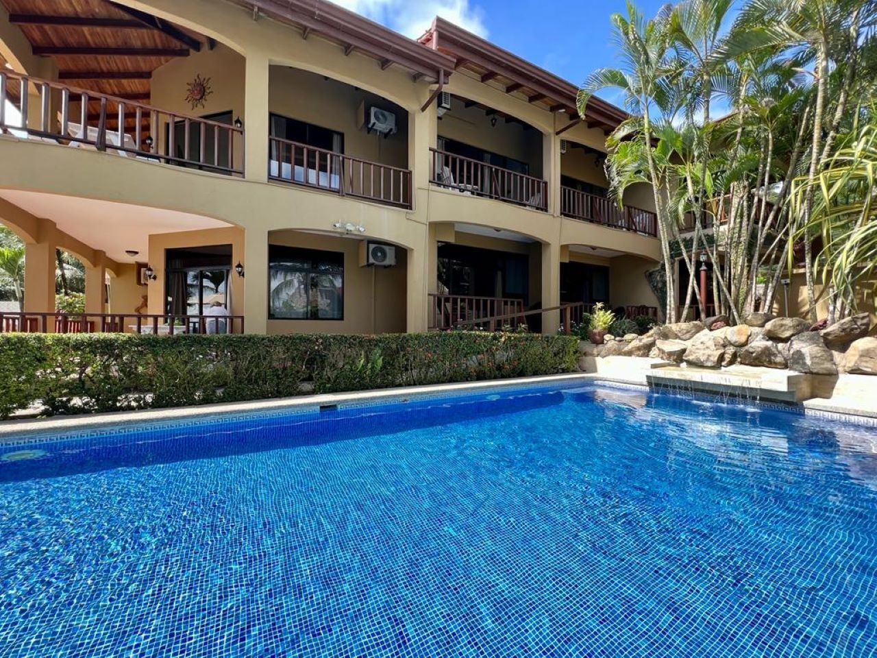 Hotel com piscina, varandas e paisagismo tropical.