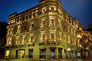 Um edifício histórico com detalhes arquitetônicos elaborados, várias varandas e janelas iluminadas à noite.