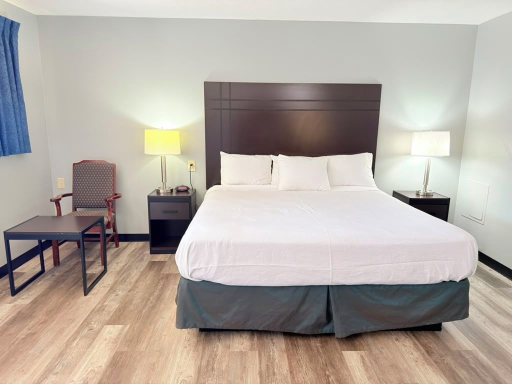 Quarto de hotel com uma cama grande, duas mesas de cabeceira com luminárias, uma escrivaninha e uma cadeira.