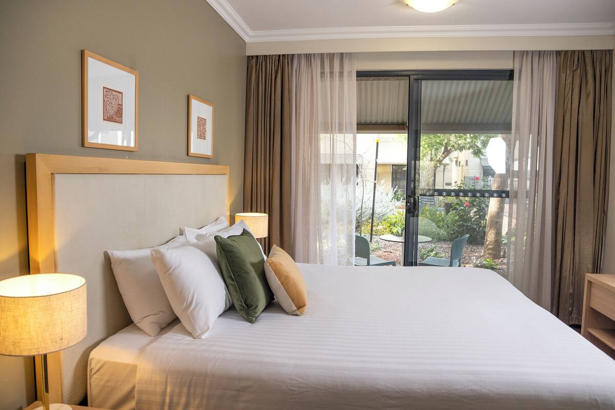 Uma cama bem arrumada com almofadas, um abajur e quadros na parede.