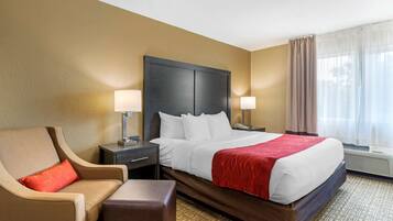 Quarto de hotel com uma cama grande, um sofá, uma mesinha de cabeceira e uma janela com cortinas.