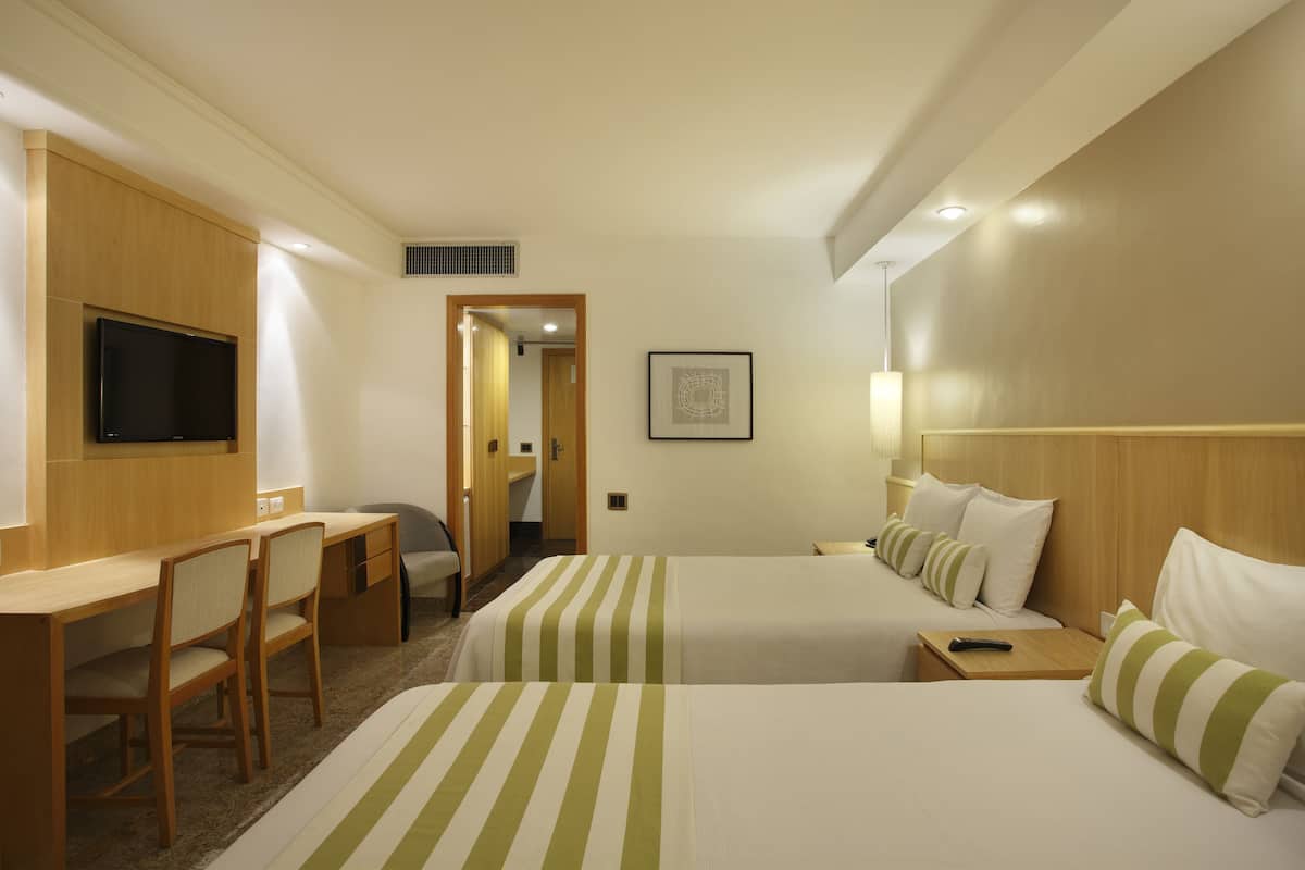 Quarto de hotel com duas camas, uma escrivaninha e uma televisão.