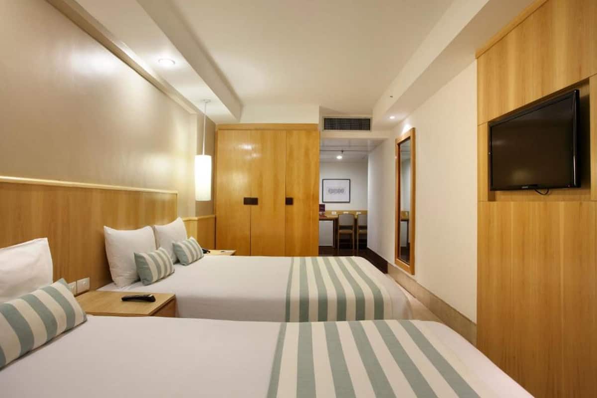 Quarto de hotel com duas camas, uma televisão, uma escrivaninha e um espelho.
