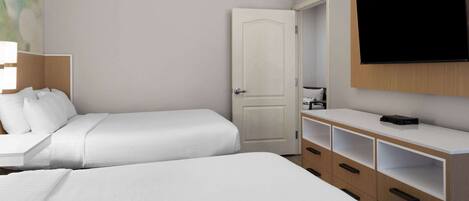 Quarto de hotel com duas camas, uma televisão fixada na parede e um armário de madeira com gavetas.