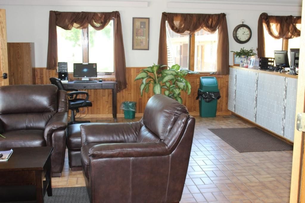 Uma sala de estar com móveis de couro, uma escrivaninha com computador e uma planta grande.