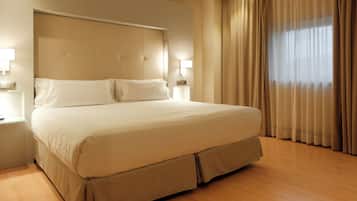 Quarto de hotel com uma cama grande, cabeceira, luminárias de cabeceira e uma janela com cortinas.