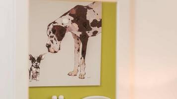Uma obra de arte emoldurada com um cão e um filhote numa parede, com uma cabeceira branca e almofadas verdes.