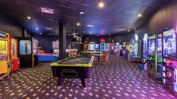 Mesa de bilhar no centro, com máquinas de arcade ao redor.