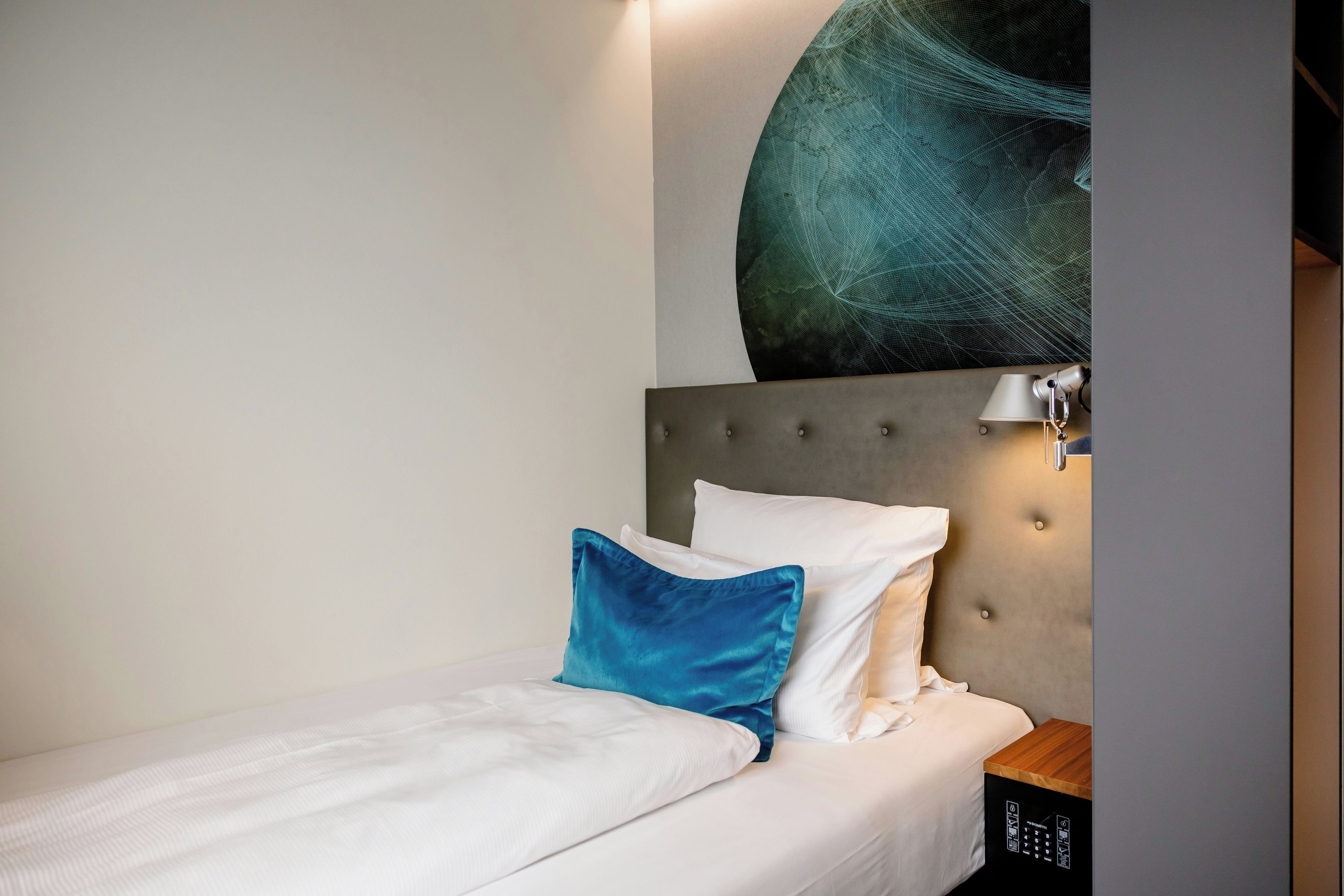 Uma cama de solteiro com cabeceira cinzenta, roupa de cama branca e travesseiro azul.