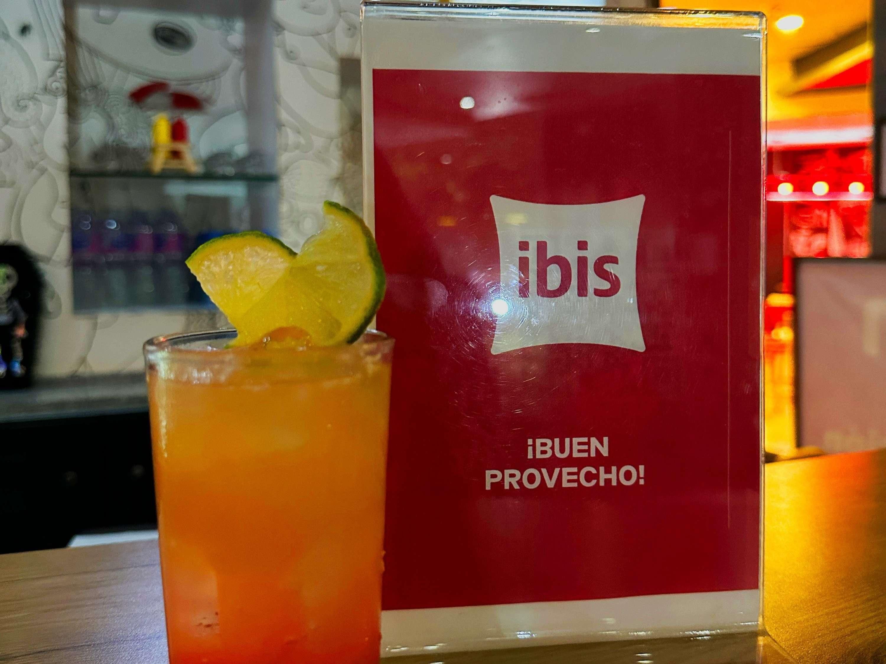 Uma área de bar com uma bebida e um letreiro com os dizeres 'ibis' e 'BUEN PROVECHO!'