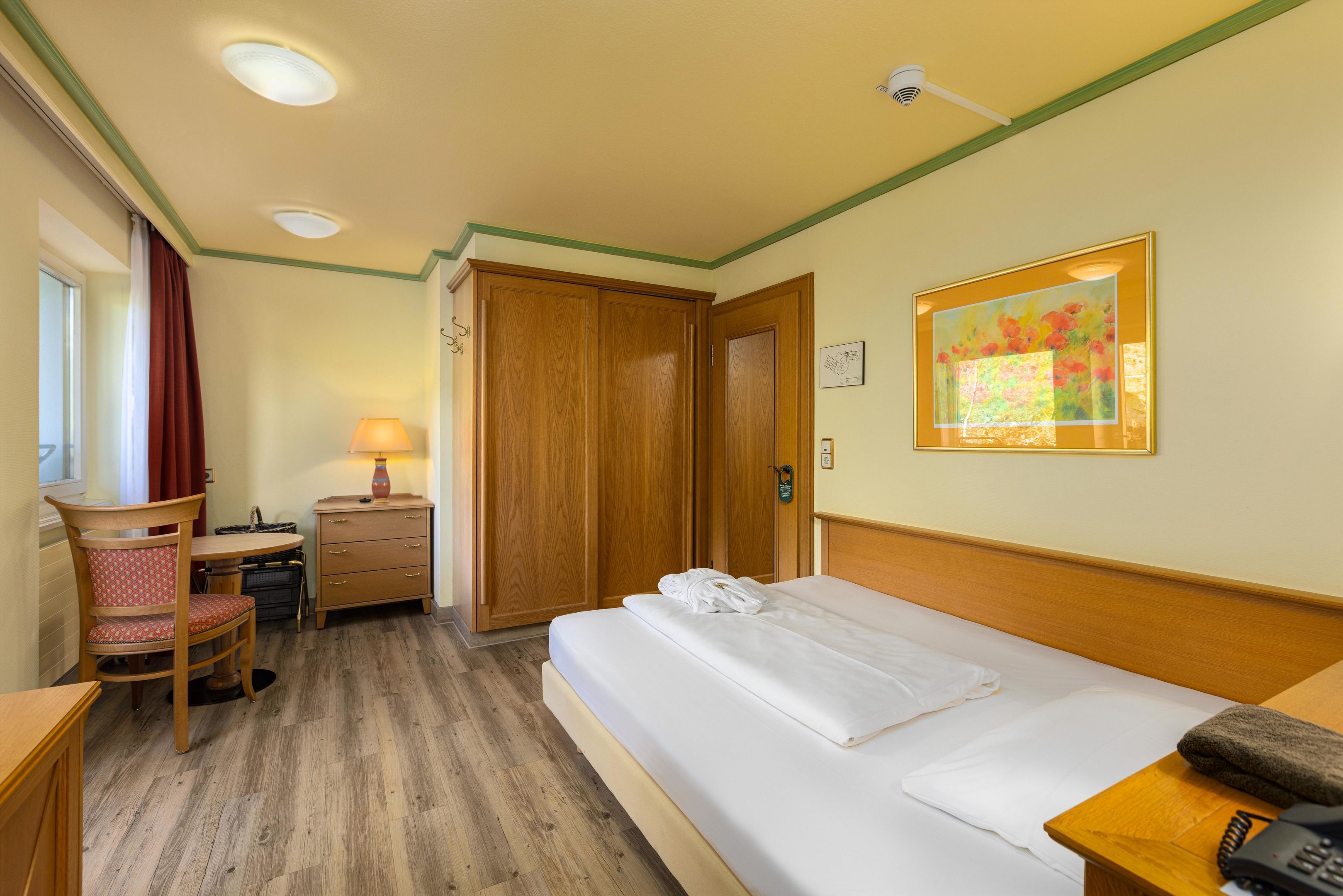 Quarto de hotel com cama, escrivaninha, cadeira e um quadro na parede.