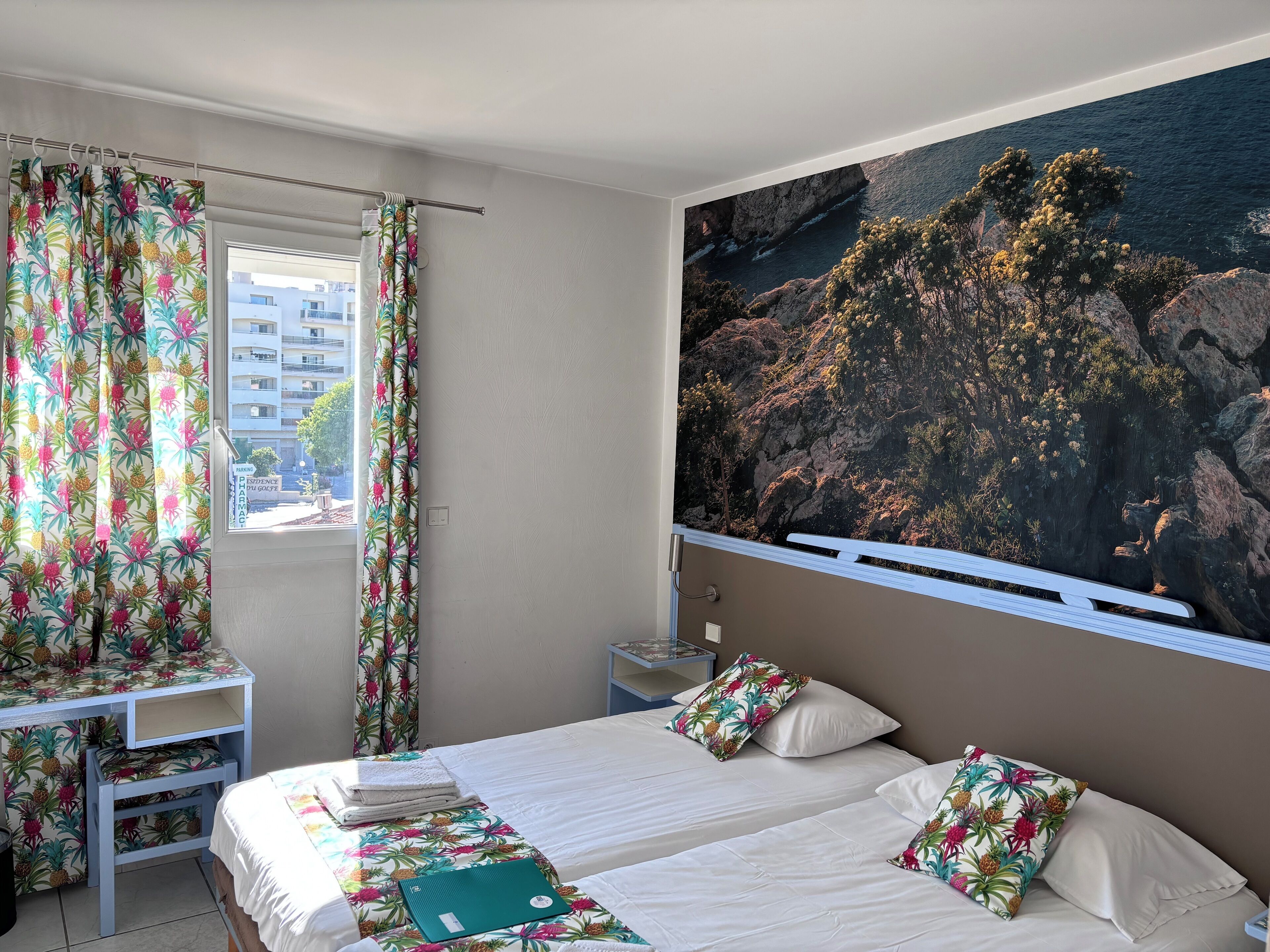 Quarto com cama, almofadas, escrivaninha e janela com cortinas.