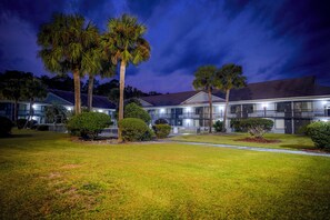 Um hotel com um gramado bem cuidado, várias palmeiras e fachada de prédio moderna.
