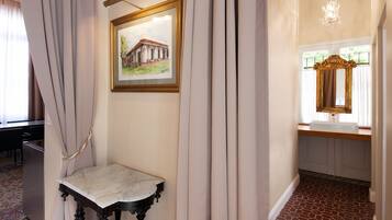 Um corredor com cortinas bege, um quadro emoldurado na parede, uma mesa de mármore e um chão estampado.