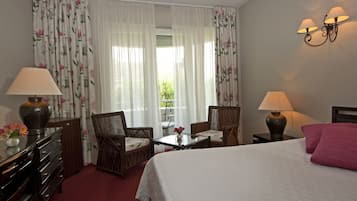 Quarto de hotel com cama, duas cadeiras, uma mesa, cômoda e duas luminárias.
