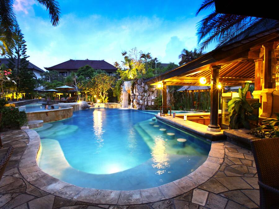 Uma piscina com borda de pedra, rodeada por espreguiçadeiras e uma área de estar coberta com vista para a piscina.