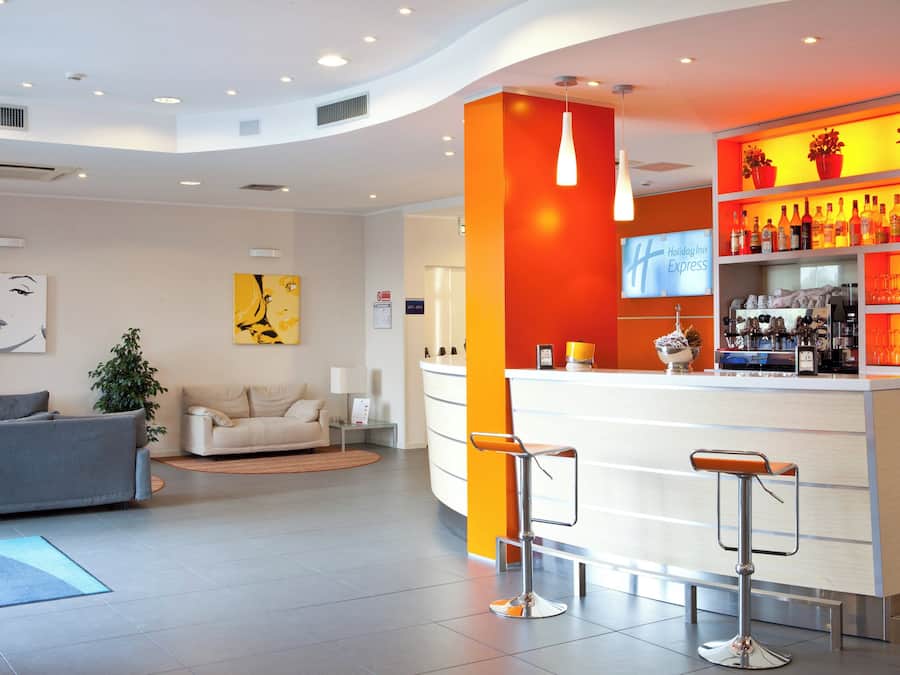 Um hall de hotel com balcão de recepção, área de bar, assentos e obras de arte nas paredes.