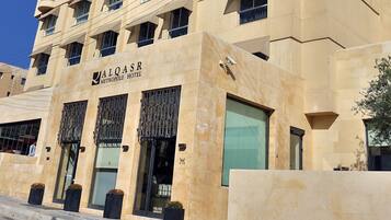Um hotel com fachada moderna, grandes janelas e uma placa com o nome 'ALQASR METROPOLENE HOTEL'.