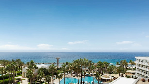 Um resort com piscina, palmeiras e vista para o oceano.