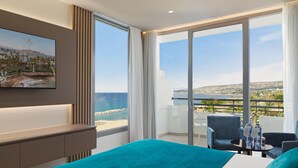 Quarto de hotel com uma cama grande, televisão fixada na parede e varanda com vista para o mar.