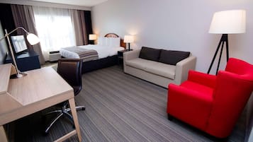 Quarto de hotel com cama, escrivaninha, poltrona vermelha, sofá e abajur.