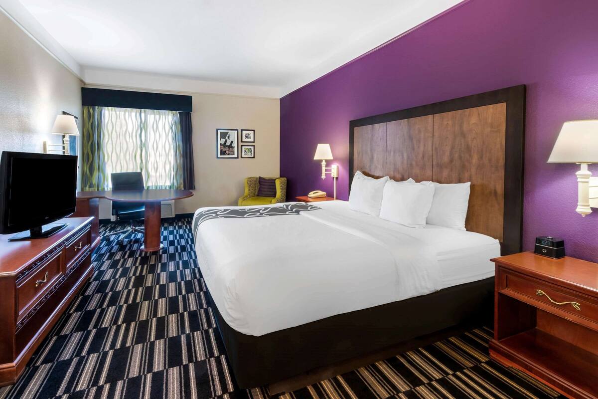Quarto de hotel com uma cama grande, televisão, escrivaninha e cadeira.
