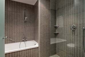 Um banheiro com chuveiro revestido em azulejos e uma banheira.