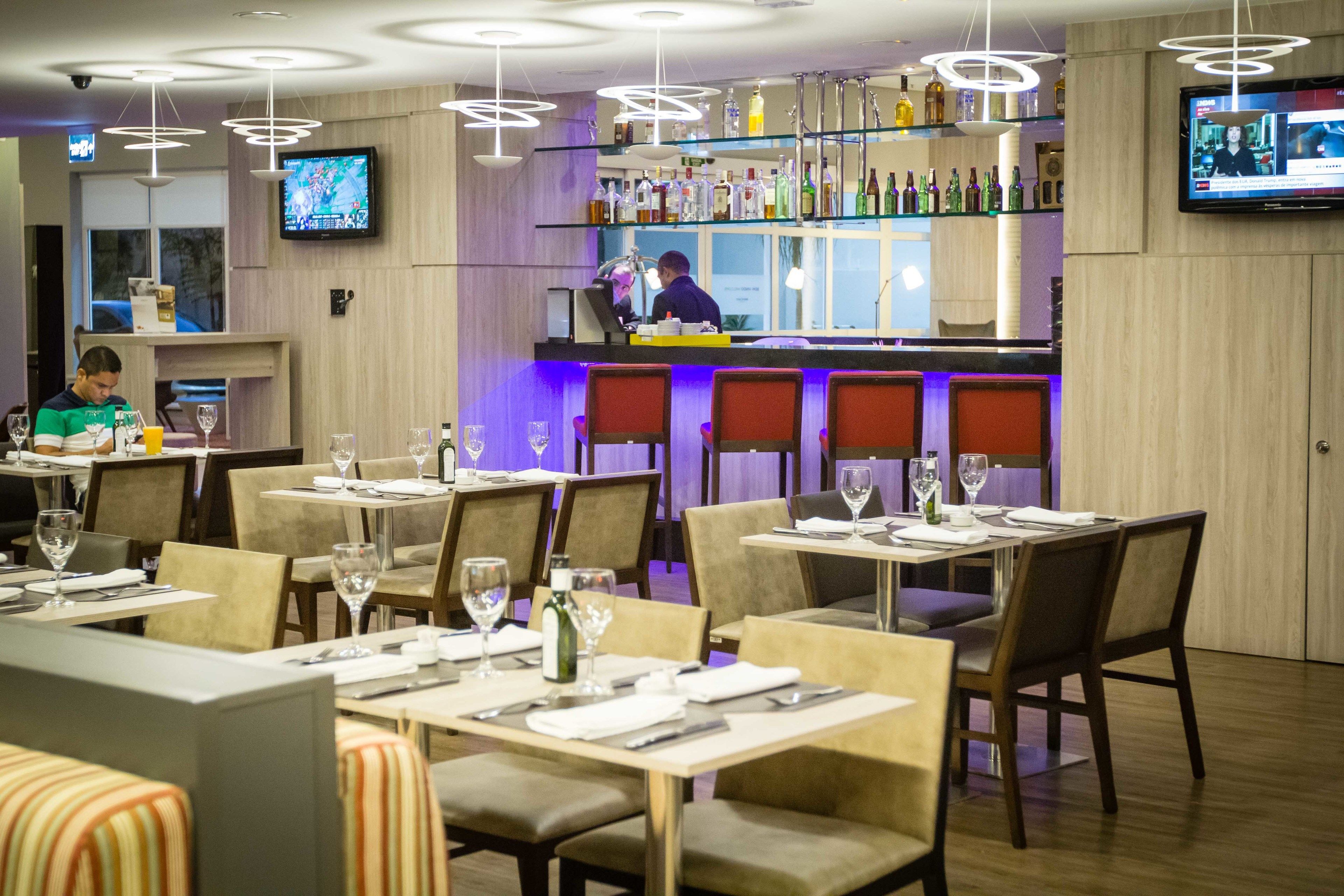 Um restaurante com várias mesas, cadeiras e um espaço de bar.