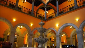 Pátio interior com uma fonte central, arcos e uma varanda com grades.