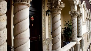 Entrada de um edifício com colunas ornamentadas e uma porta de madeira escura.