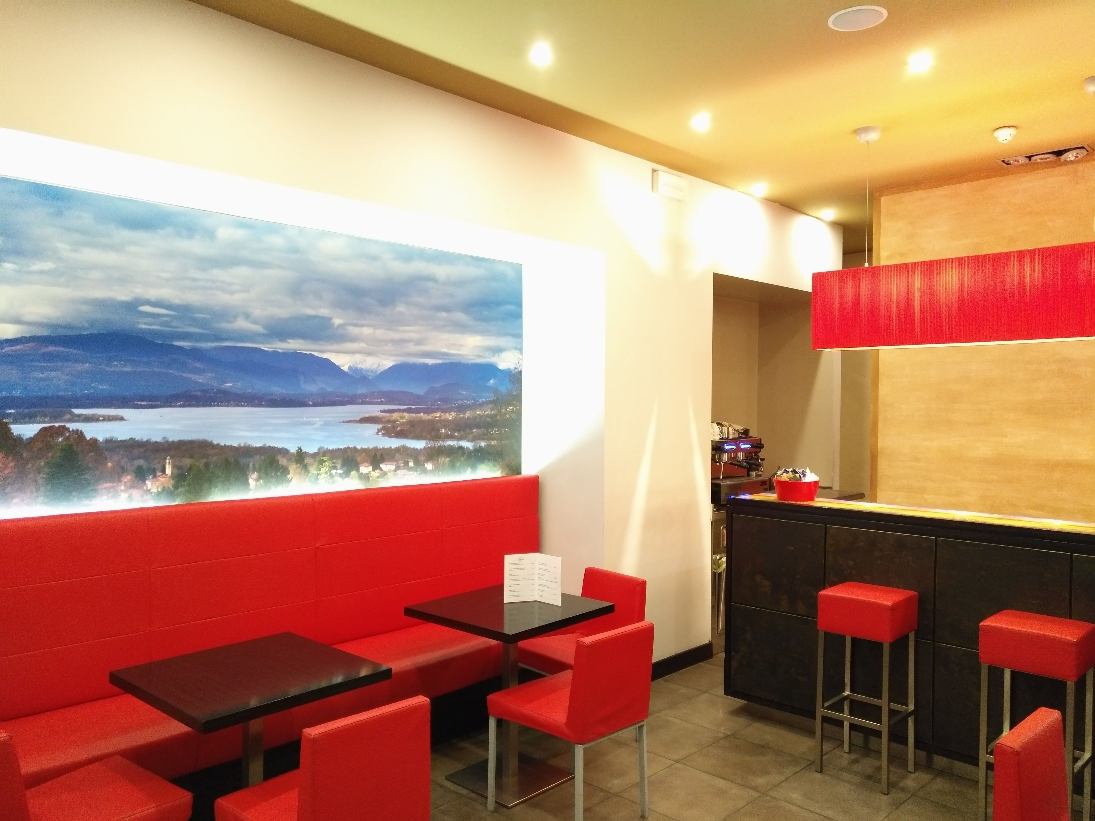Restaurante com assentos vermelhos, mesa preta e uma grande janela com vista panorâmica para montanhas e um lago.