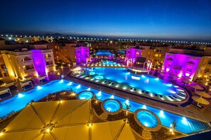 Uma grande piscina ao ar livre com vários ofurôs, cercada por edifícios com varandas iluminadas.