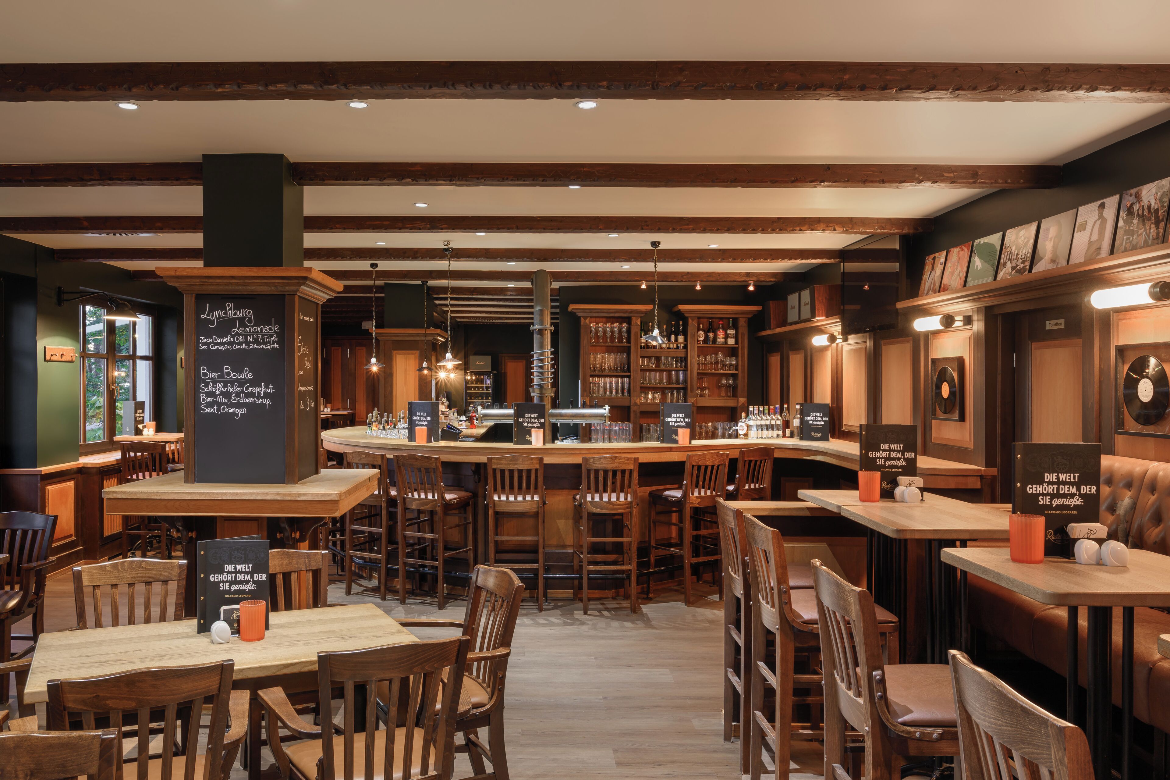 Um restaurante acolhedor com mesas e cadeiras de madeira, um espaço de bar e um cardápio em lousa.