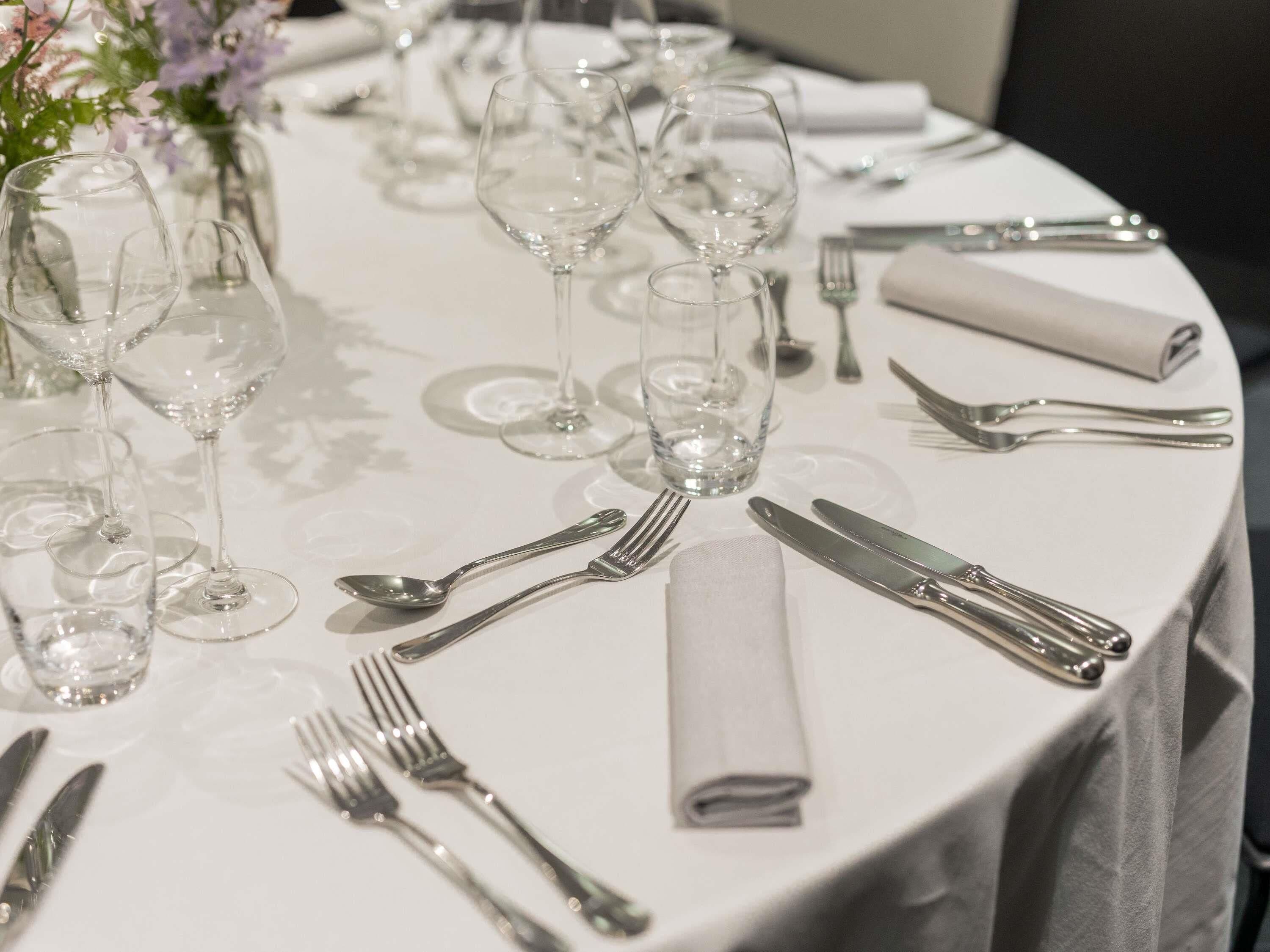 Mesa posta com taças de vinho, talheres e guardanapos dobrados, indicando um arranjo de jantar formal.