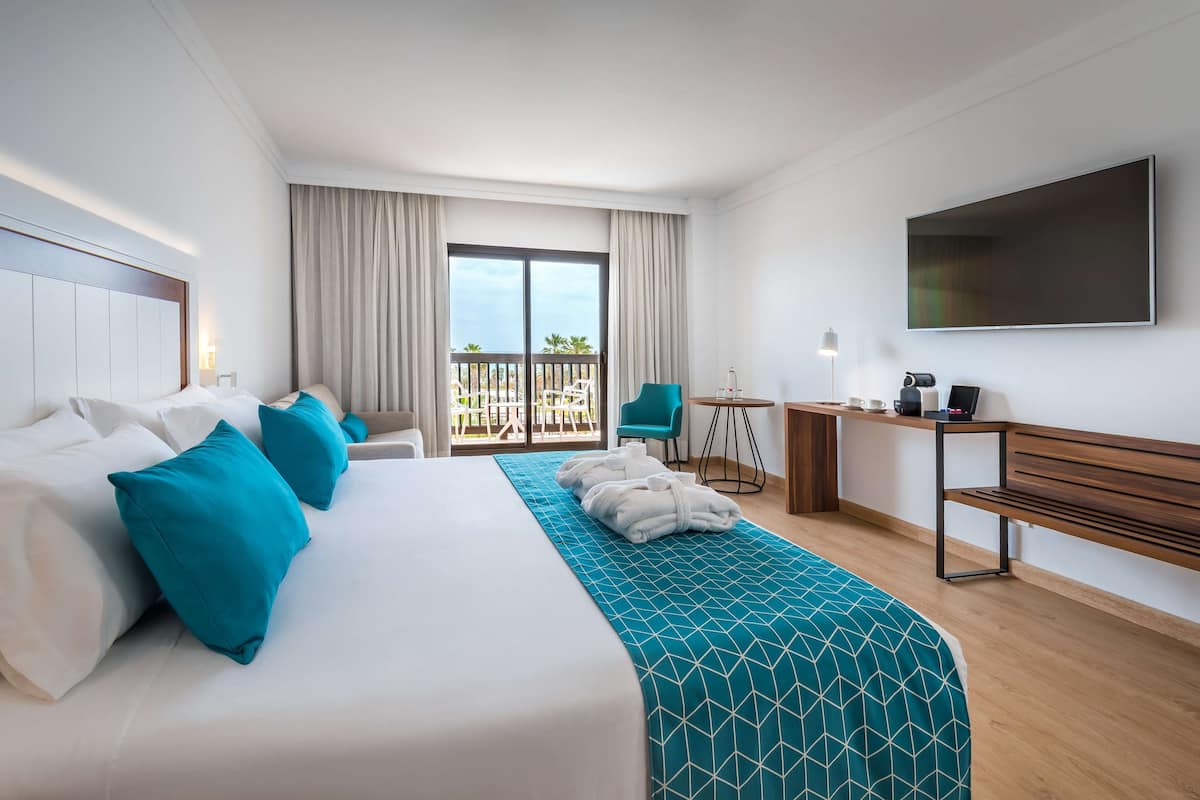 Quarto de hotel com uma cama grande, uma escrivaninha, uma cadeira e uma televisão.